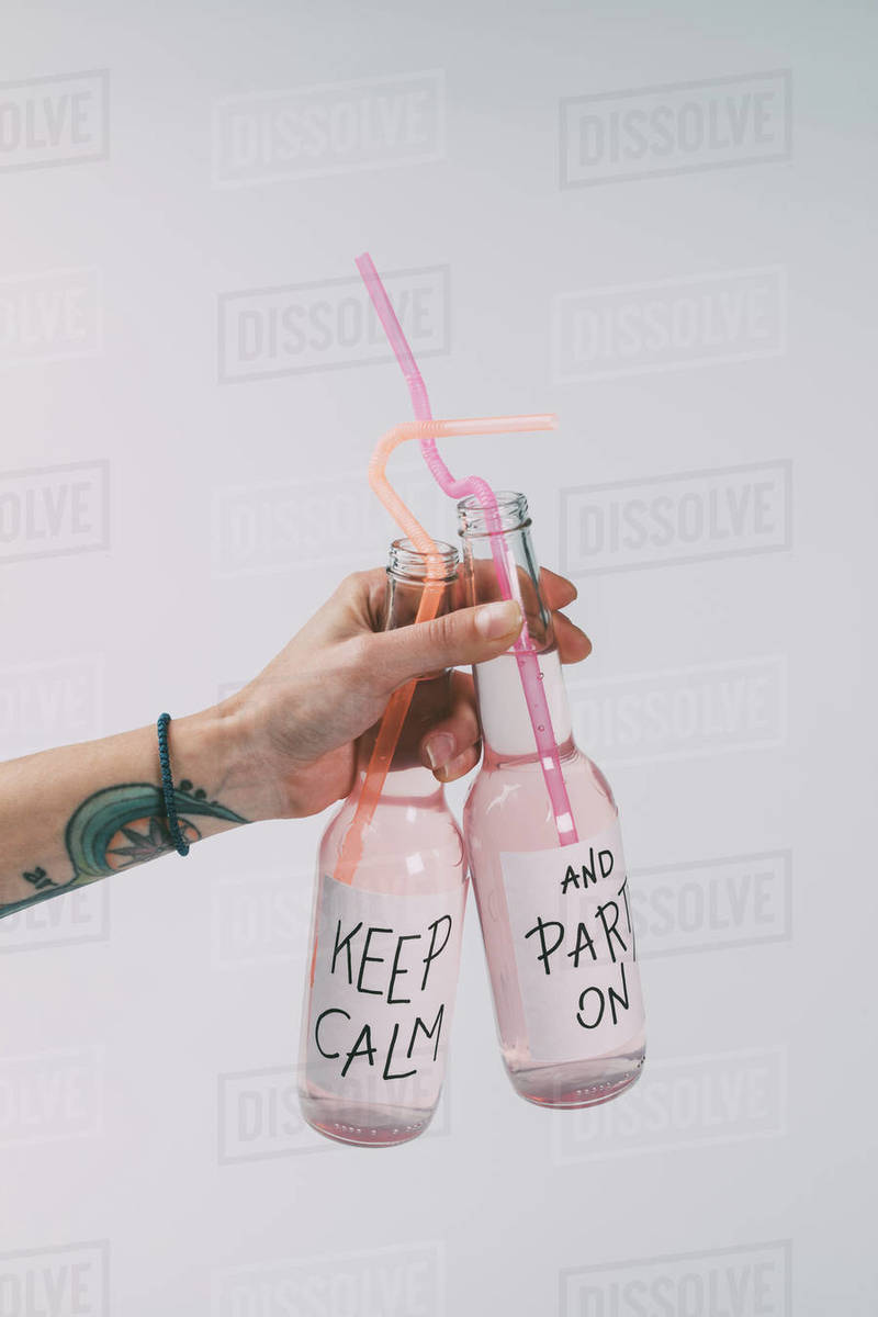 Close-up view of bottles of alcohol beverages with straws in hand ...