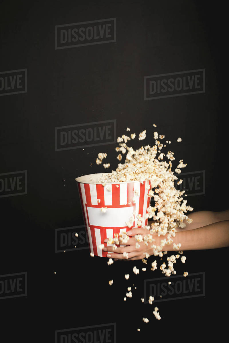 Cropped shot of woman holding bucket of spilling popcorn isolated on ...