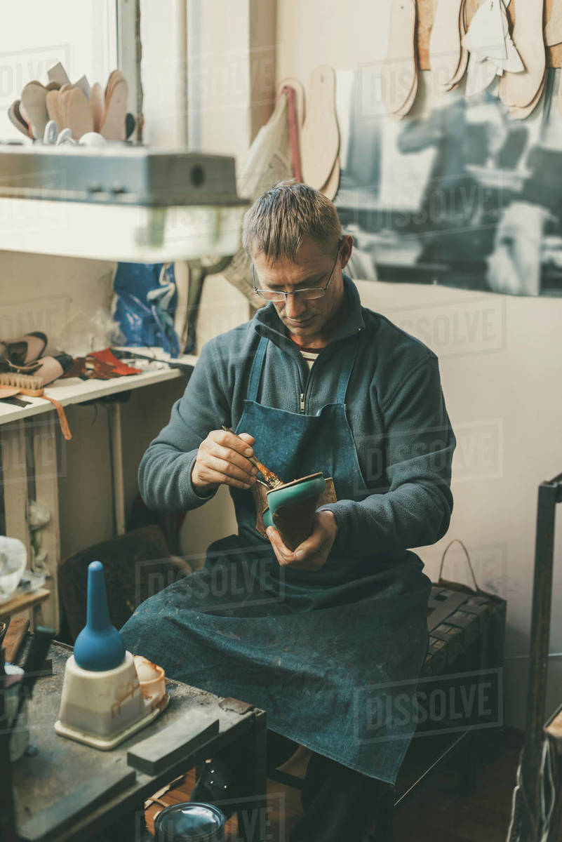 Mature cobbler holding boot workpiece and working with sole while ...