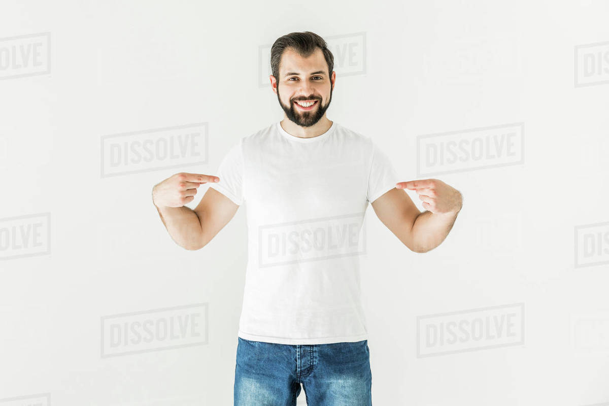 Handsome young man pointing at white t-shirt and smiling at camera ...
