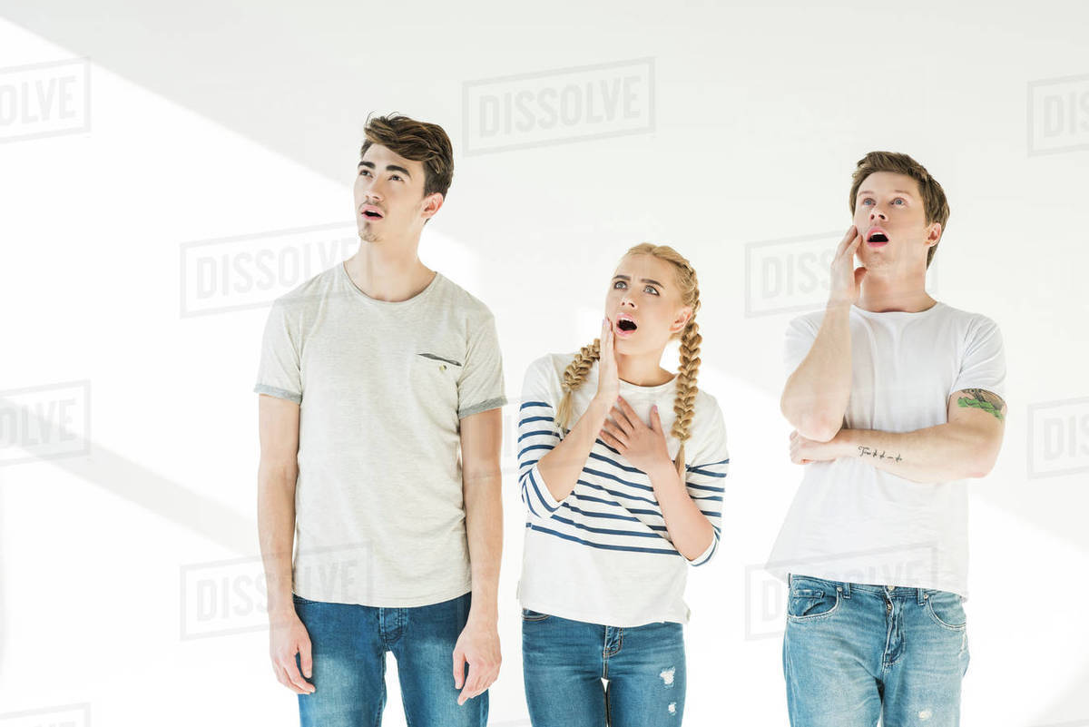Young shocked friends standing together and looking away on grey ...