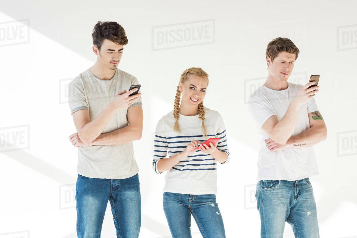 Smiling young people using smartphones while standing together on grey ...