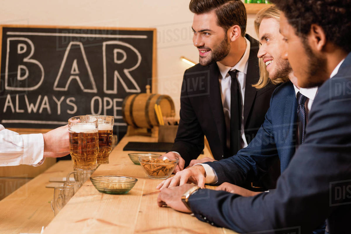Cropped shot of bartender giving glasses of beer with smiling ...