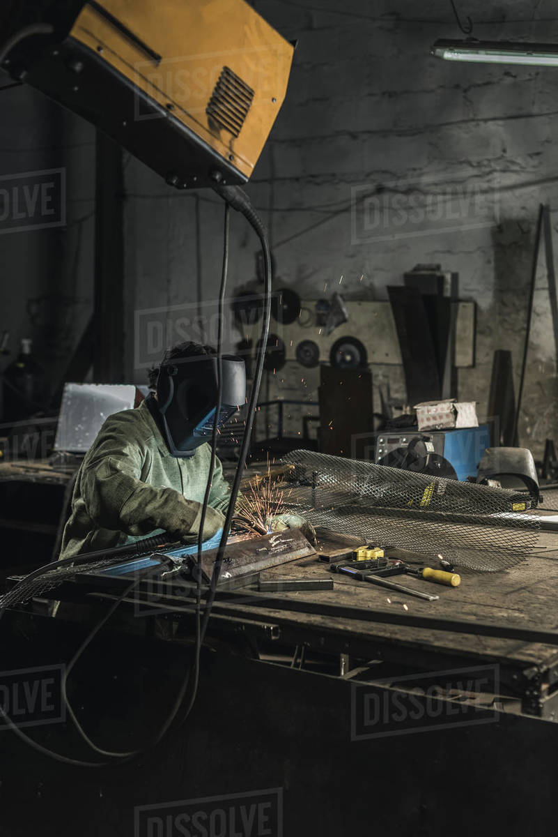 Side view of welder in protective work wear working with welding torch ...