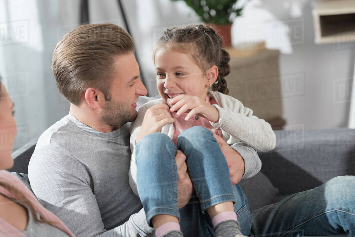 Young father playing around with his little daughter on couch in living ...