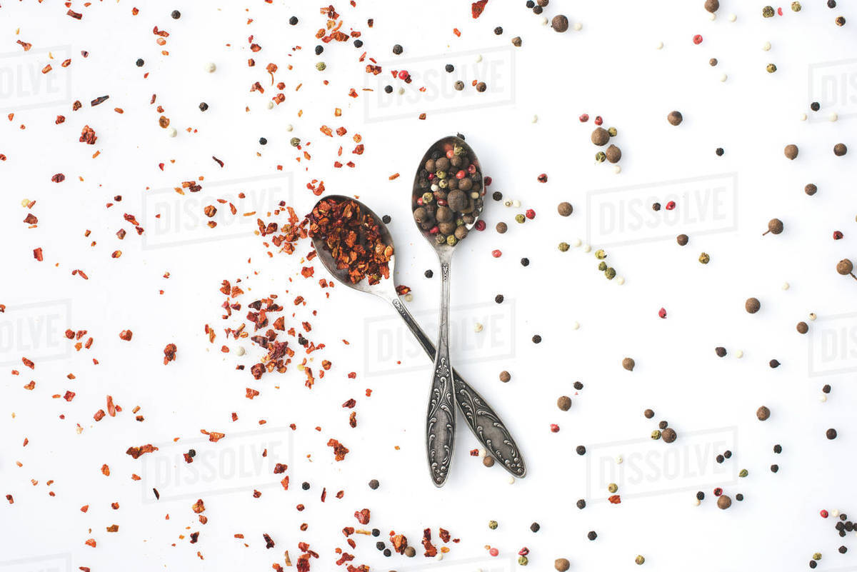 top view of crossed spoons with pepper spilled isolated on white ...