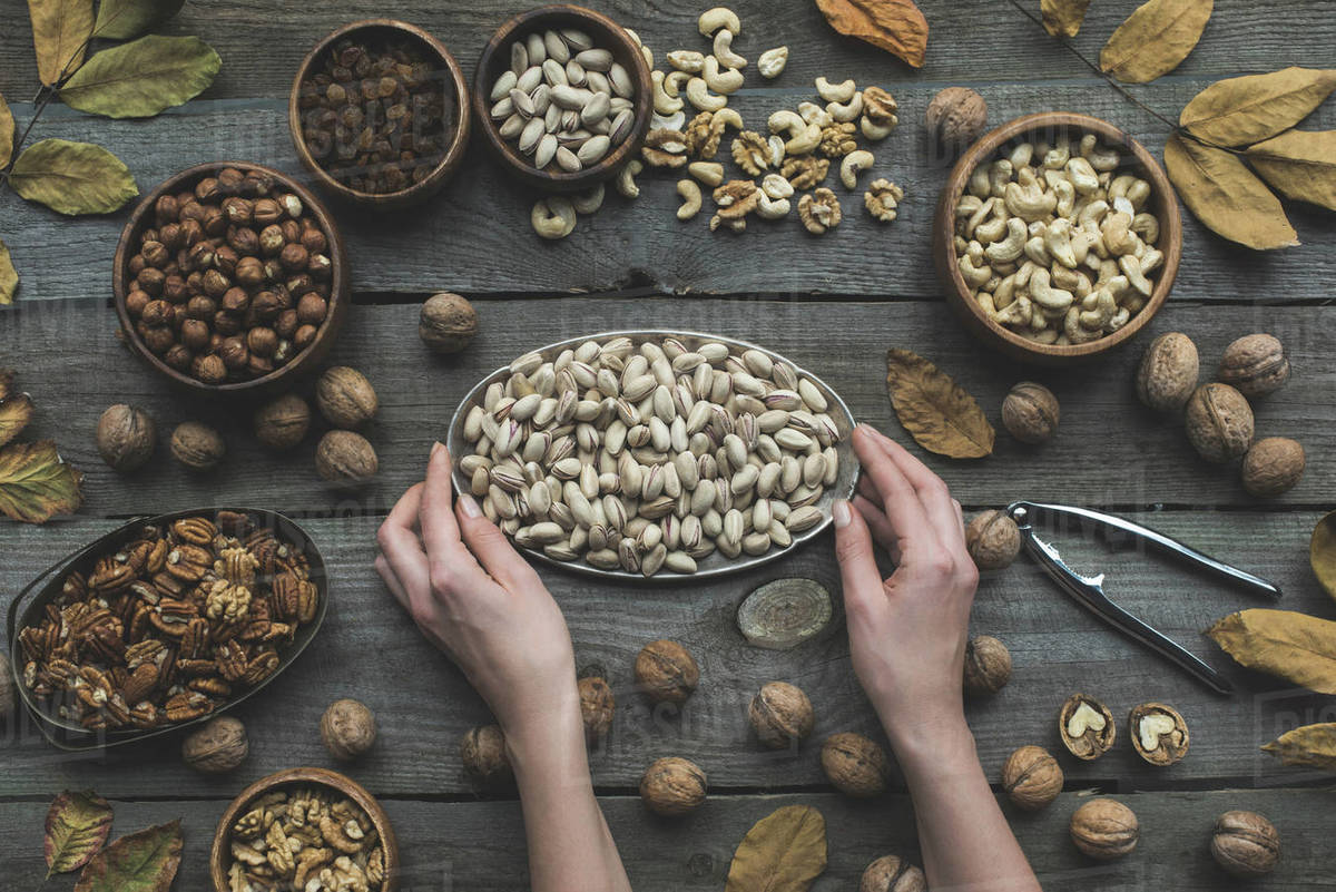 Top view of human hands and various nuts in bowls with dried autumn ...