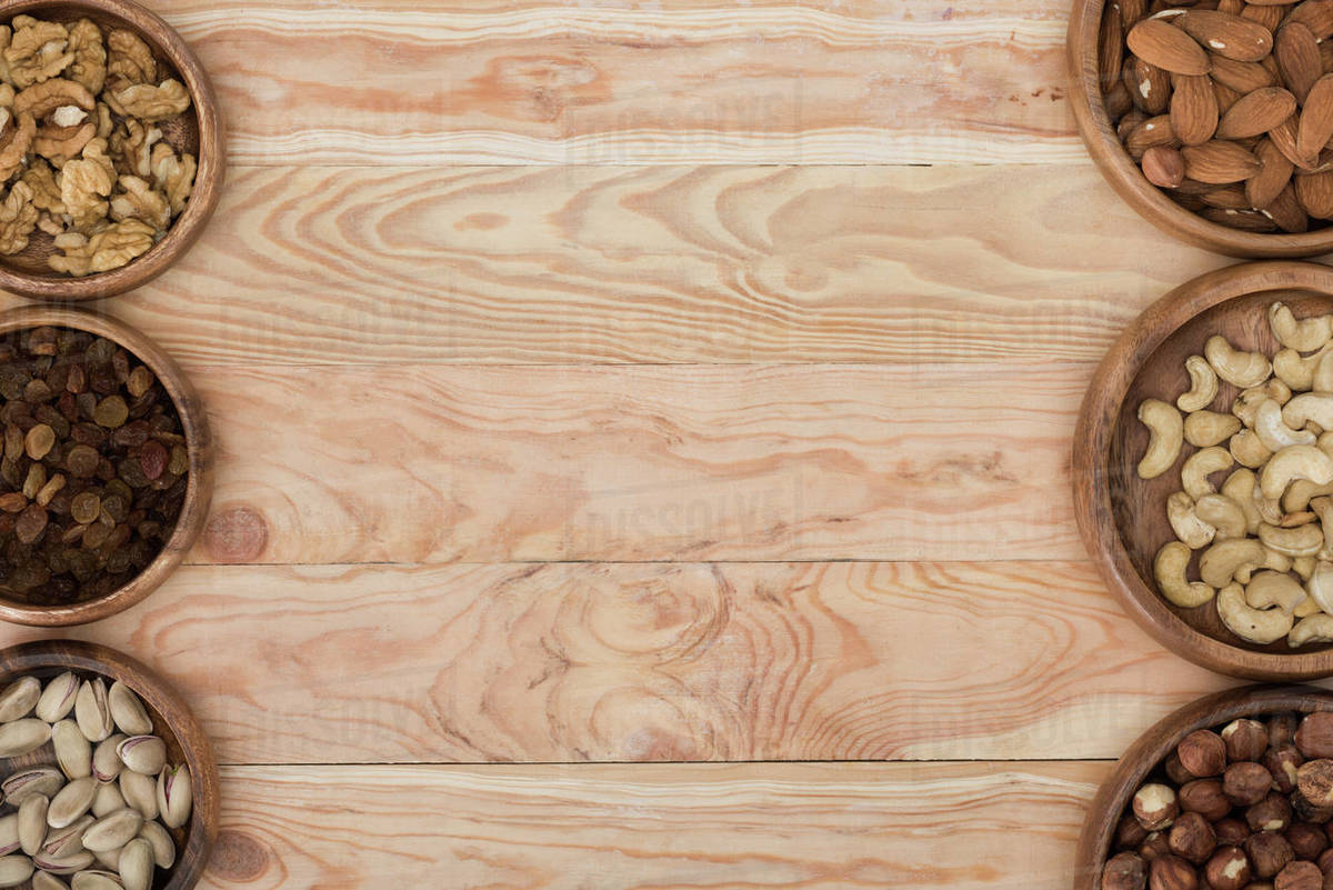 Top view of assorted nuts in bowls on wooden table - Stock Photo - Dissolve