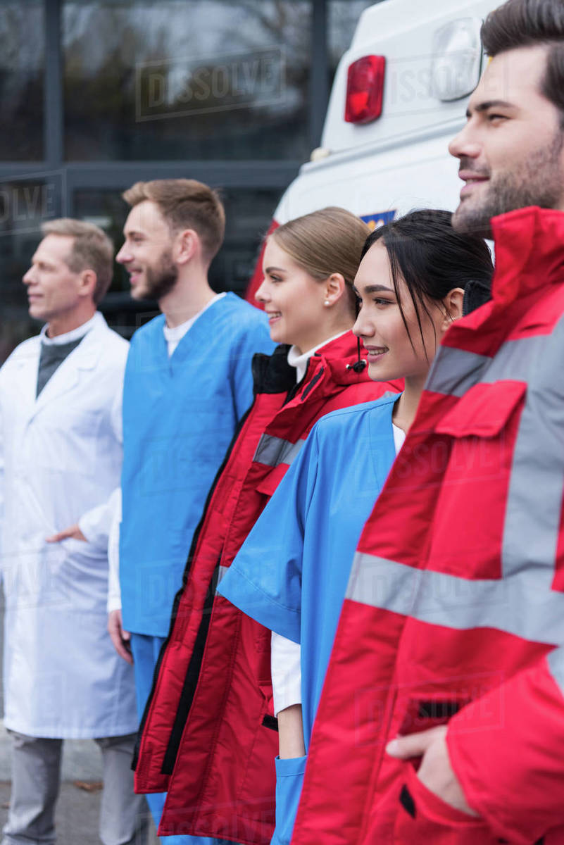 Side view of paramedics working team standing in front of car - Royalty ...