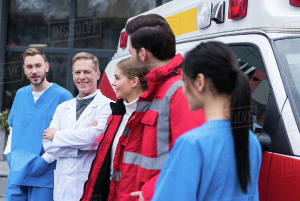 Paramedics working team standing in front of car and looking at each ...