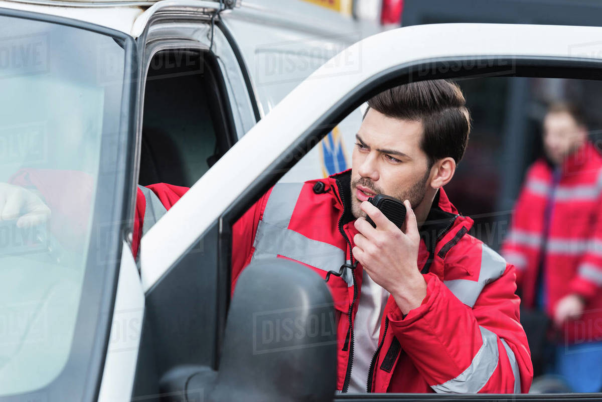 Young handsome male paramedic standing near ambulance and talking by ...