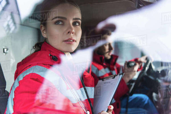 Attractive young paramedic sitting in ambulance and looking away ...
