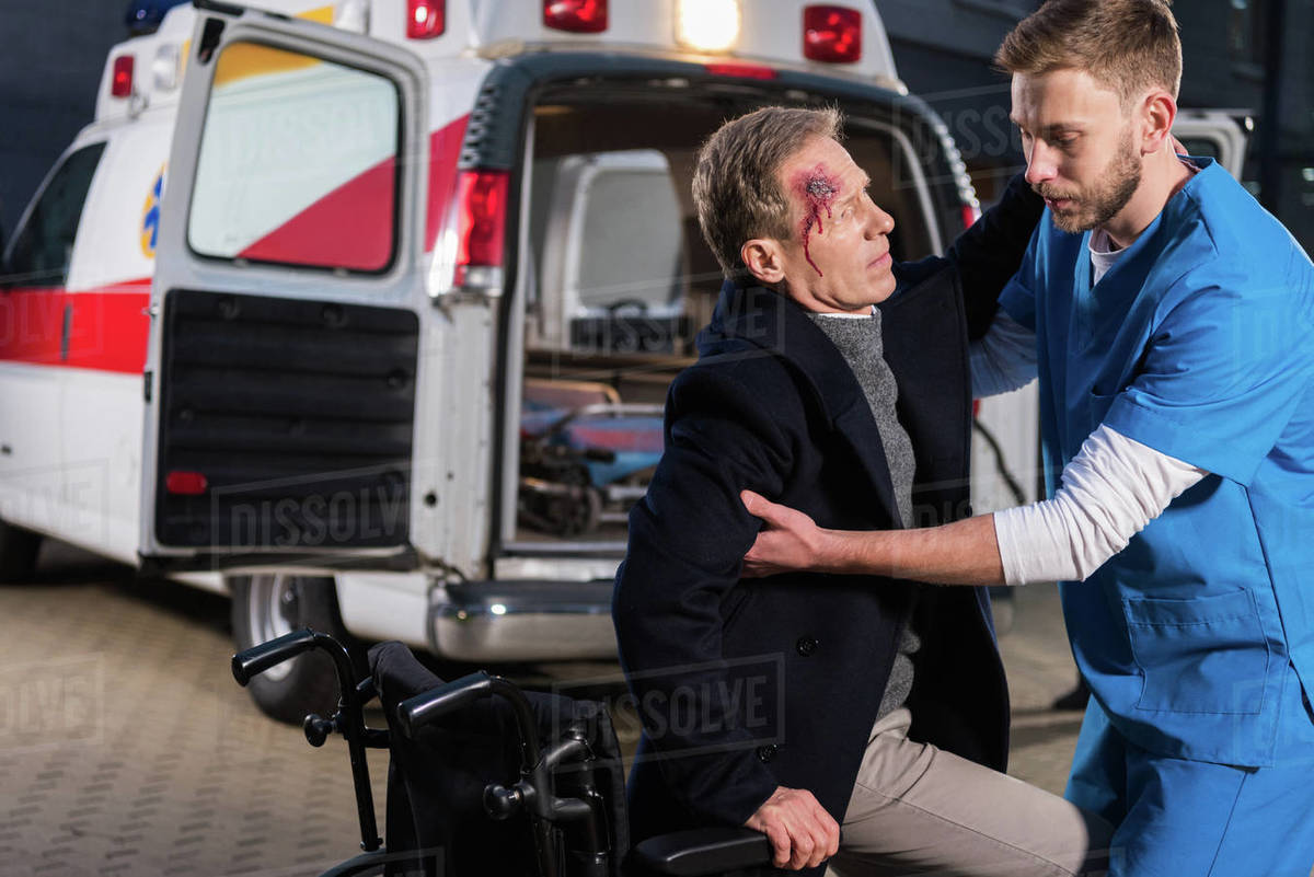 Paramedic helping injured man to sit on wheelchair - Royalty-free Stock ...