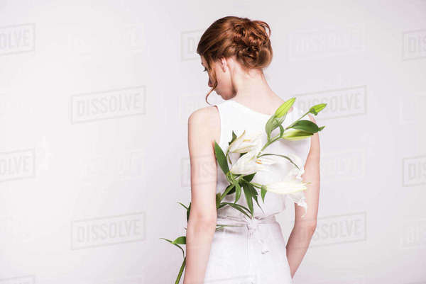 back view of young woman in white dress holding beautiful lily flowers ...
