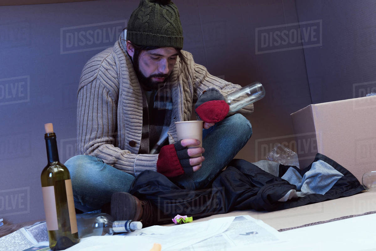 Homeless alcoholic drinking in cardboard box - Stock Photo - Dissolve