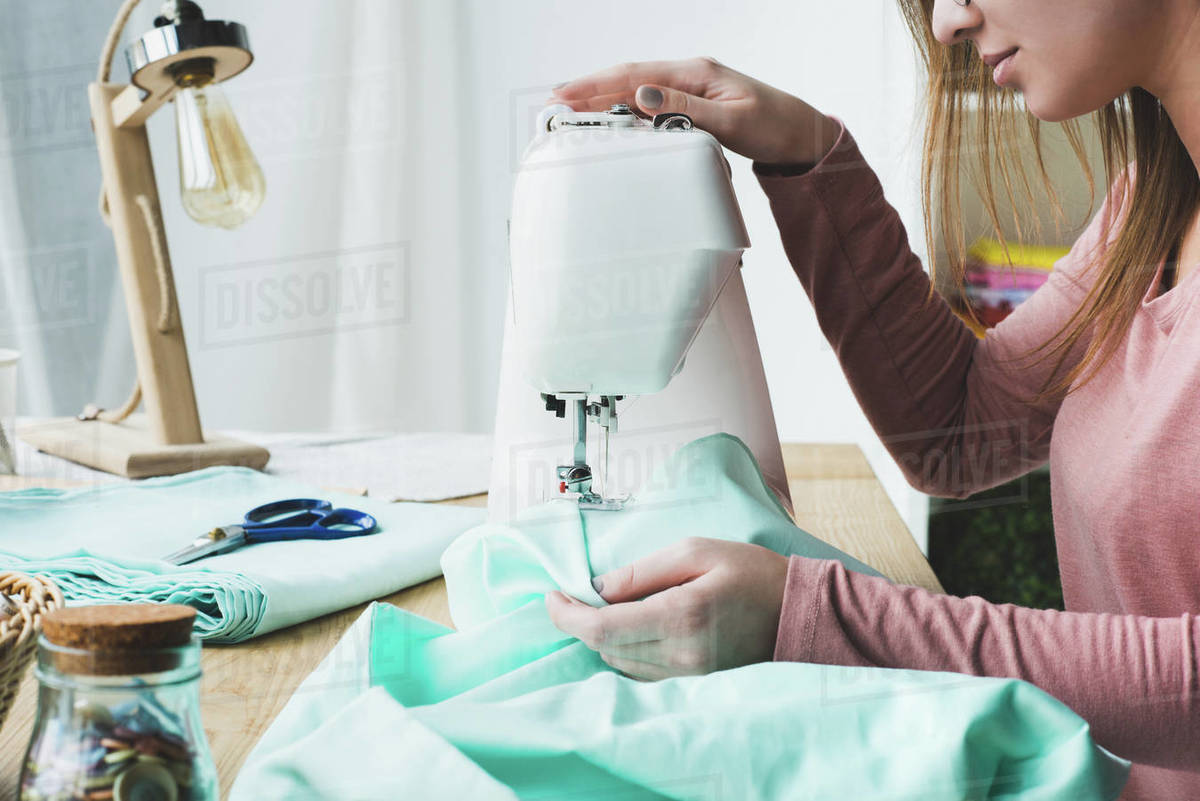 Cropped image of young seamstress using sewing machine at workplace ...