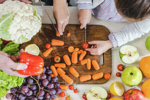 Overhead view of cropped hands slicing vegetables on chopping board at ...