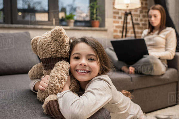 Selective focus of smiling kid hugging teddy bear and mother working on ...