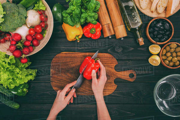 Top view of cropped hands slicing pepper by knife on chopping board ...