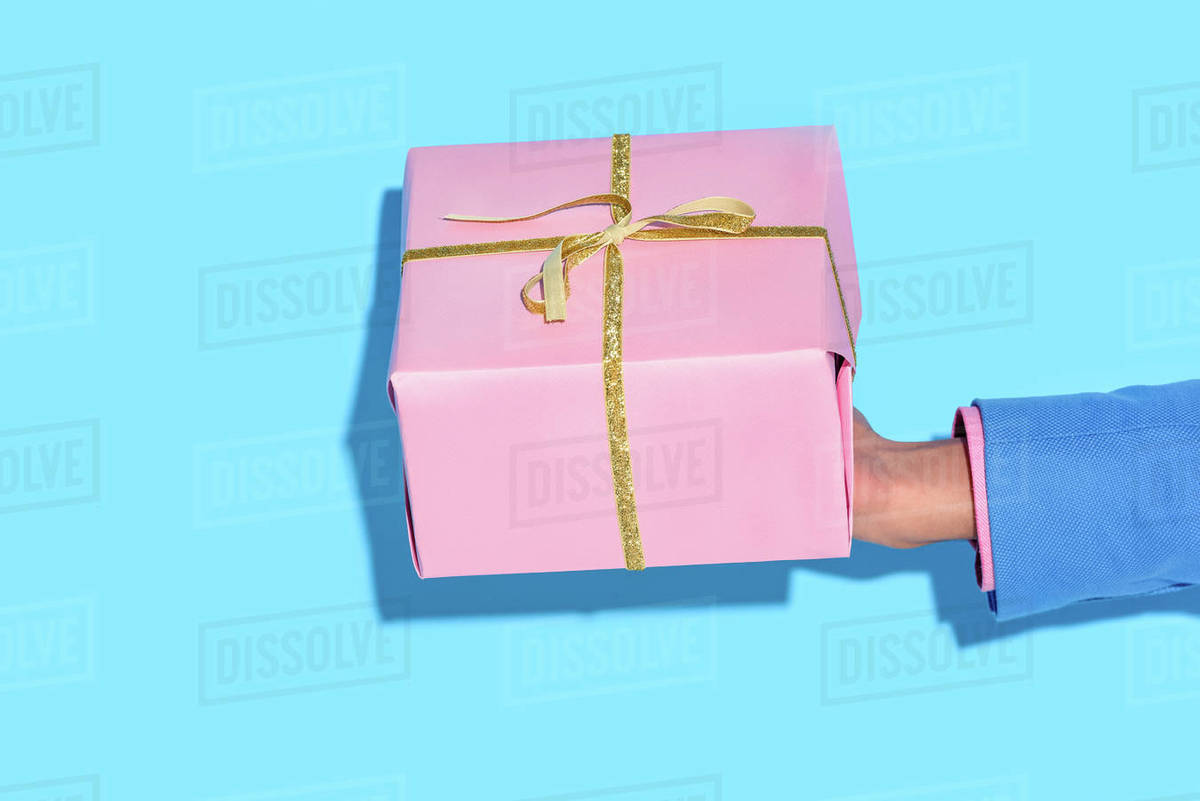 Partial view of african american man holding wrapped gift on blue wall ...