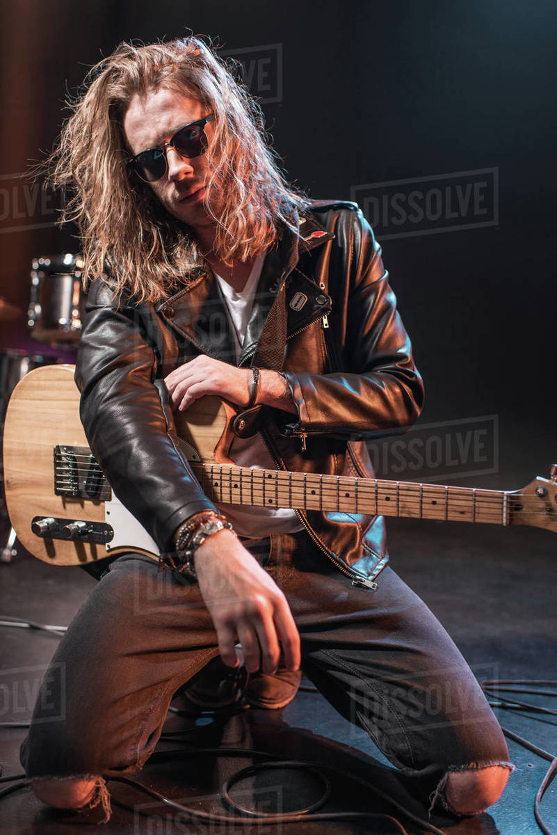 Handsome rock star in eyeglasses posing with electric guitar on stage ...