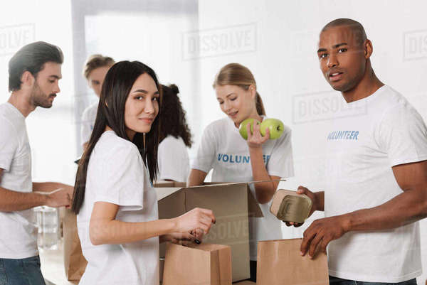 Group of multiethnic volunteers packing food into paper bags and boxes ...