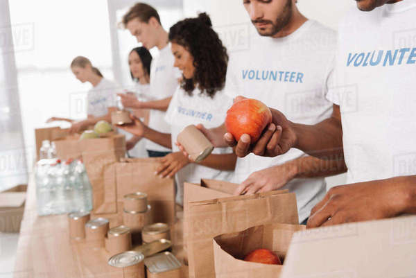 Group of multiethnic volunteers putting food and drinks into paper bags ...