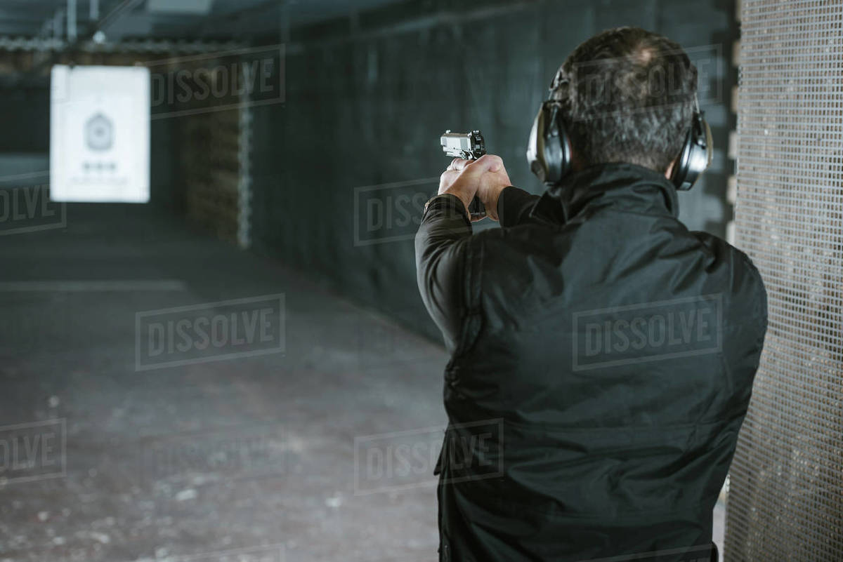 Rear view of man aiming gun at target in shooting range - Royalty-free ...