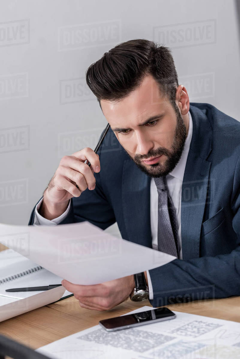 Businessman sitting at table and looking at documents with surprise ...