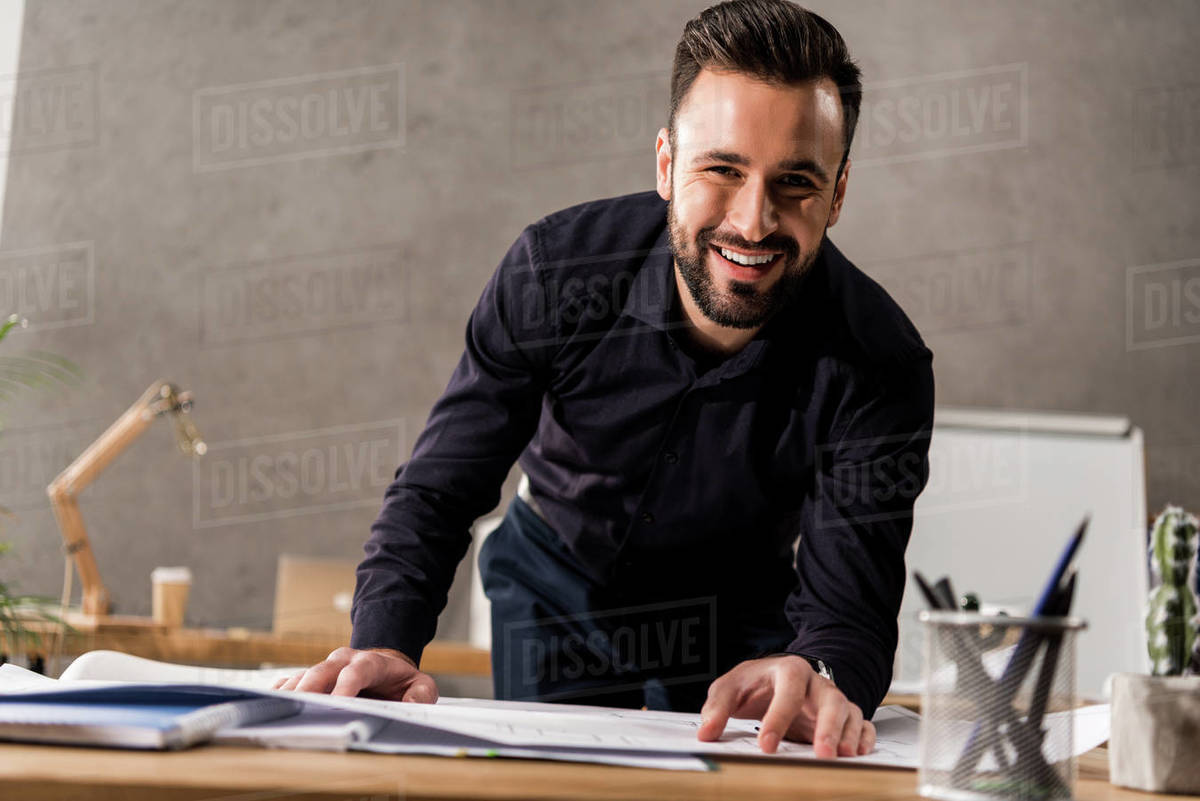Smiling architect touching blueprints and looking at camera - Royalty ...