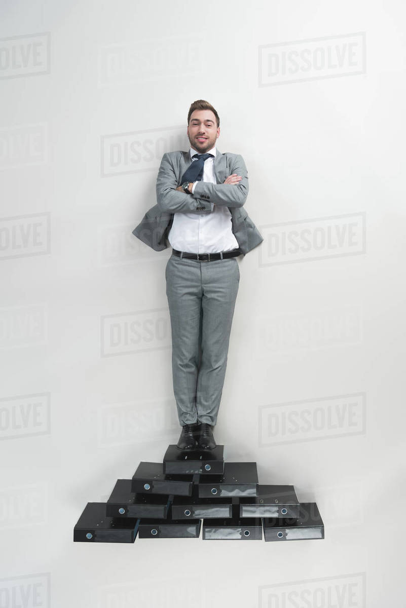Overhead view of businessman with arms crossed standing on pile of ...