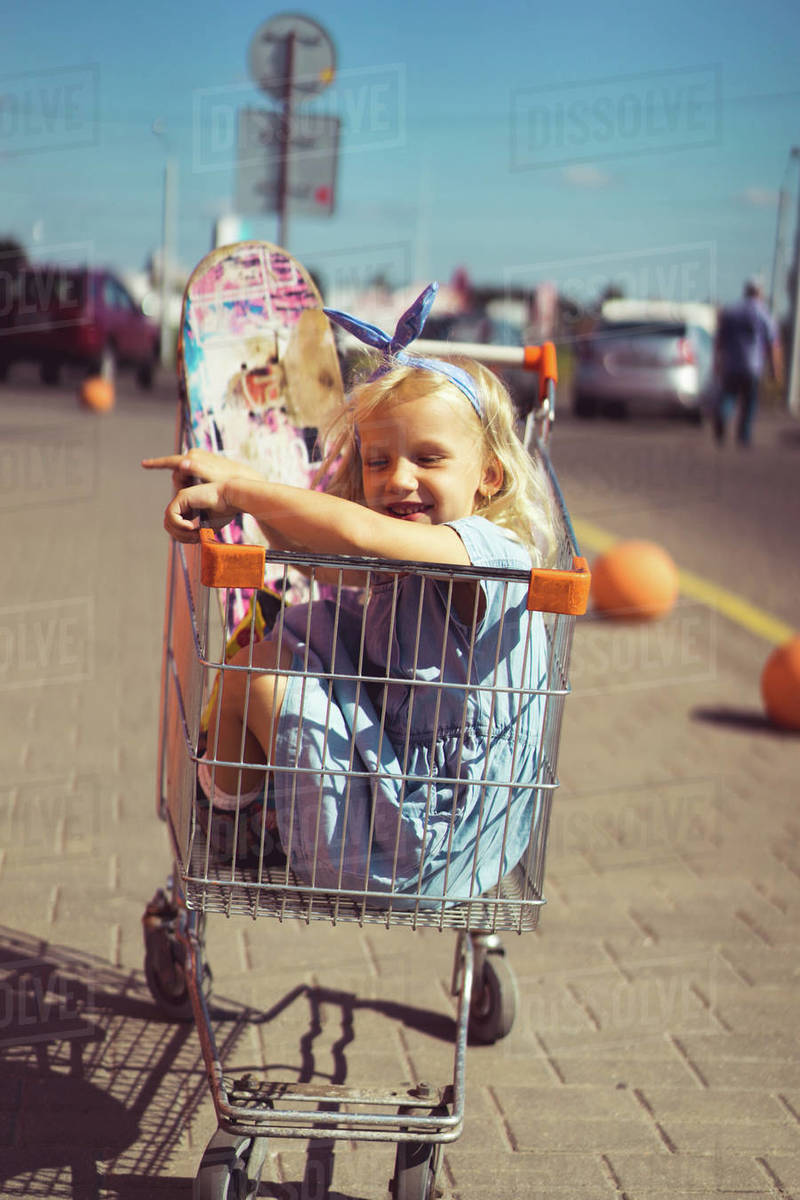 little adorable smiling kid sitting in shopping cart with skateboard ...