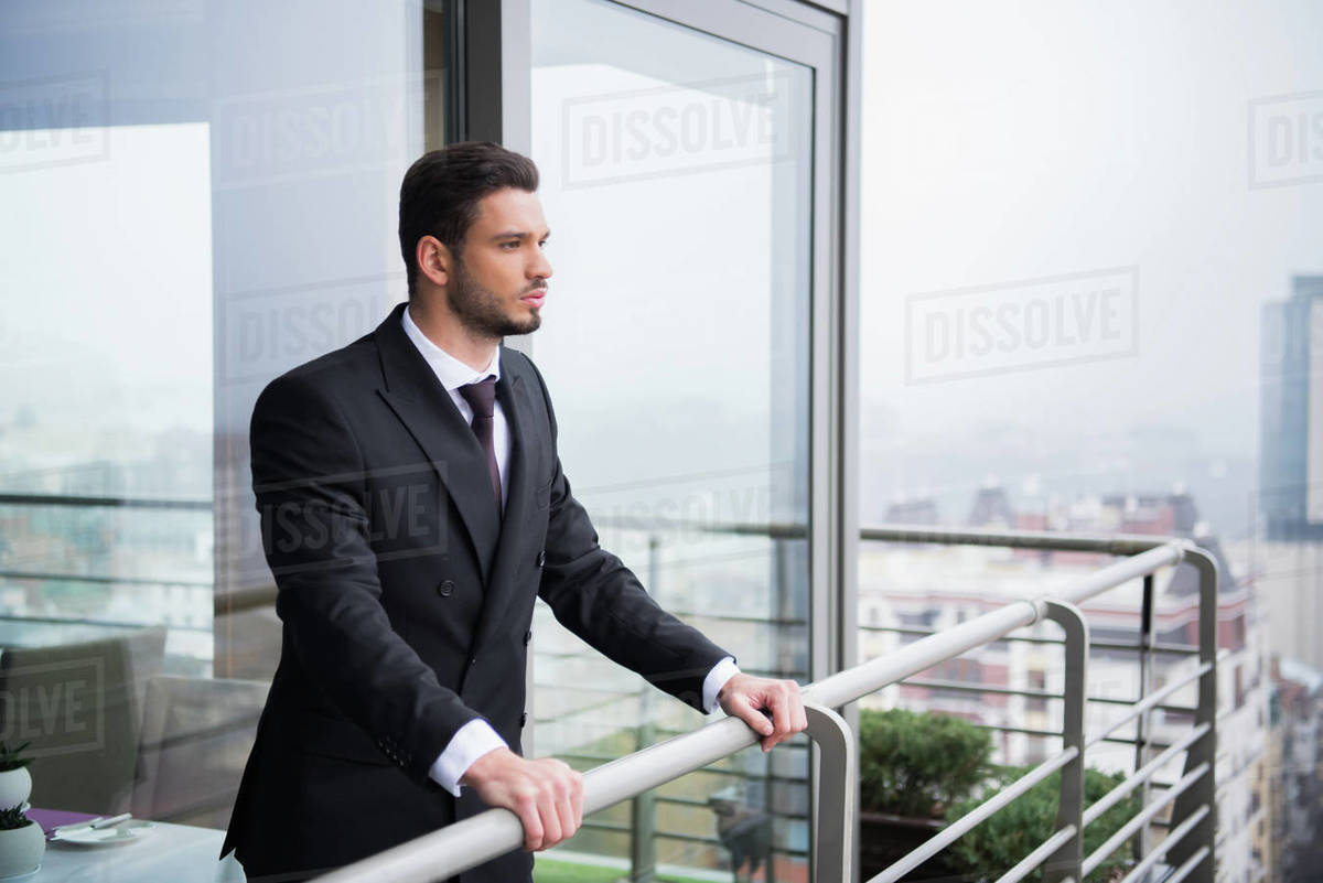 Portrait of young pensive man in suit standing at balcony - Royalty ...