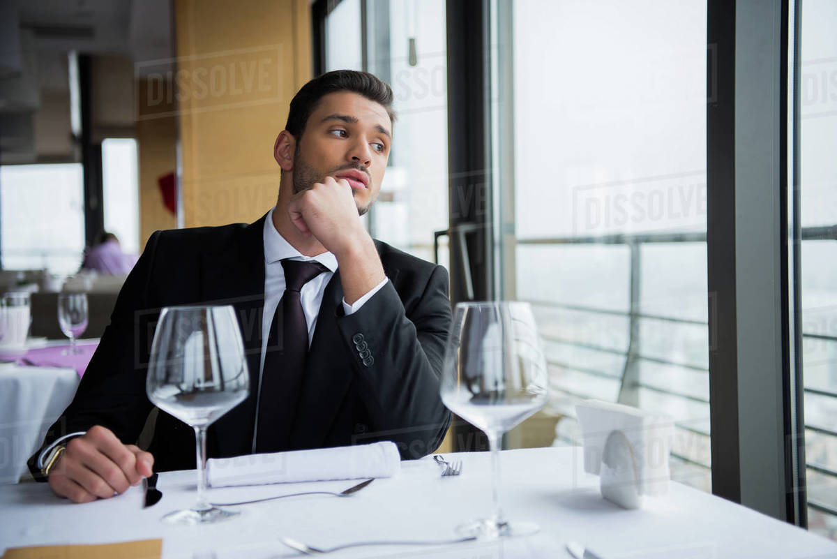 Pensive man in suit looking away while waiting for order in restaurant ...