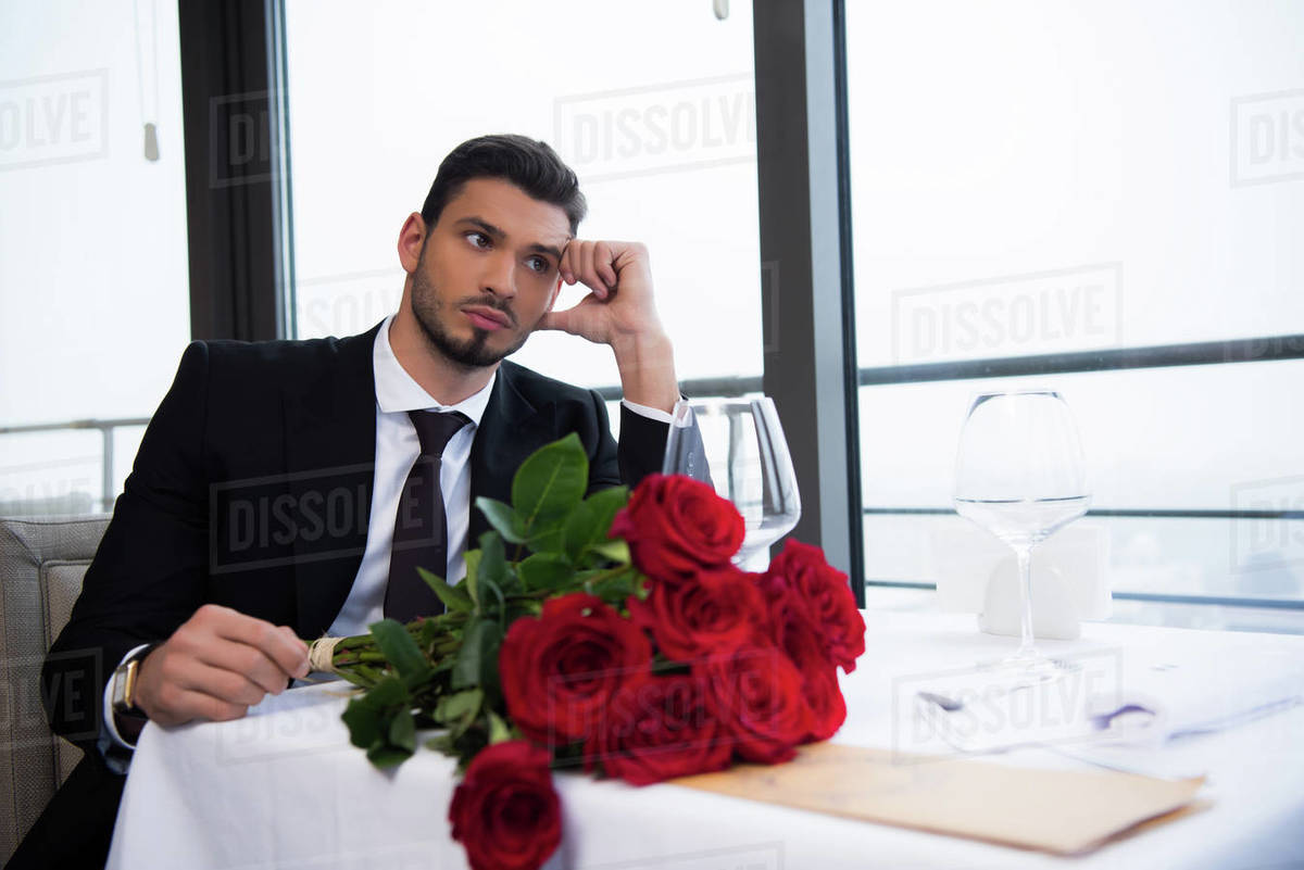 Young man in suit with bouquet of red roses waiting for girlfriend in ...