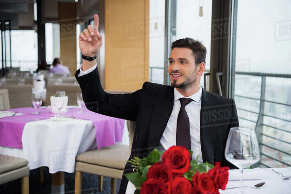 Portrait of smiling man in suit calling for waiter in restaurant ...