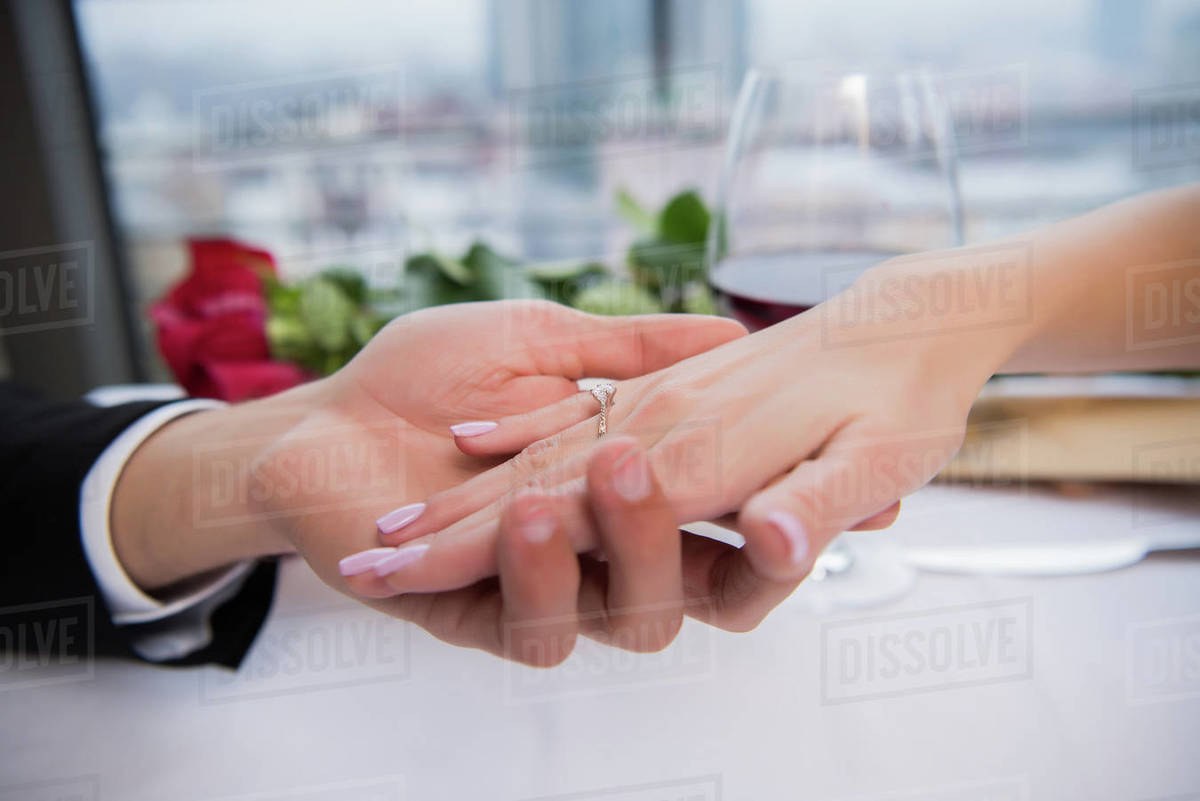 Cropped shot of boyfriend holding fiancés hand during romantic date in ...