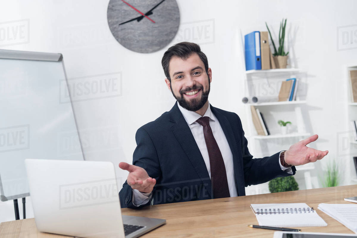 Portrait of cheerful businessman at workplace with laptop in office ...