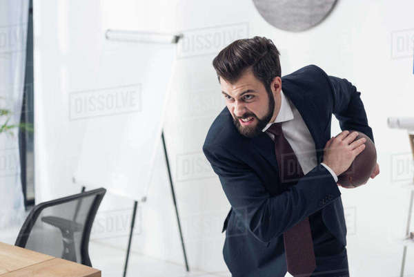 Side view of angry businessman in suit playing rugby in office ...