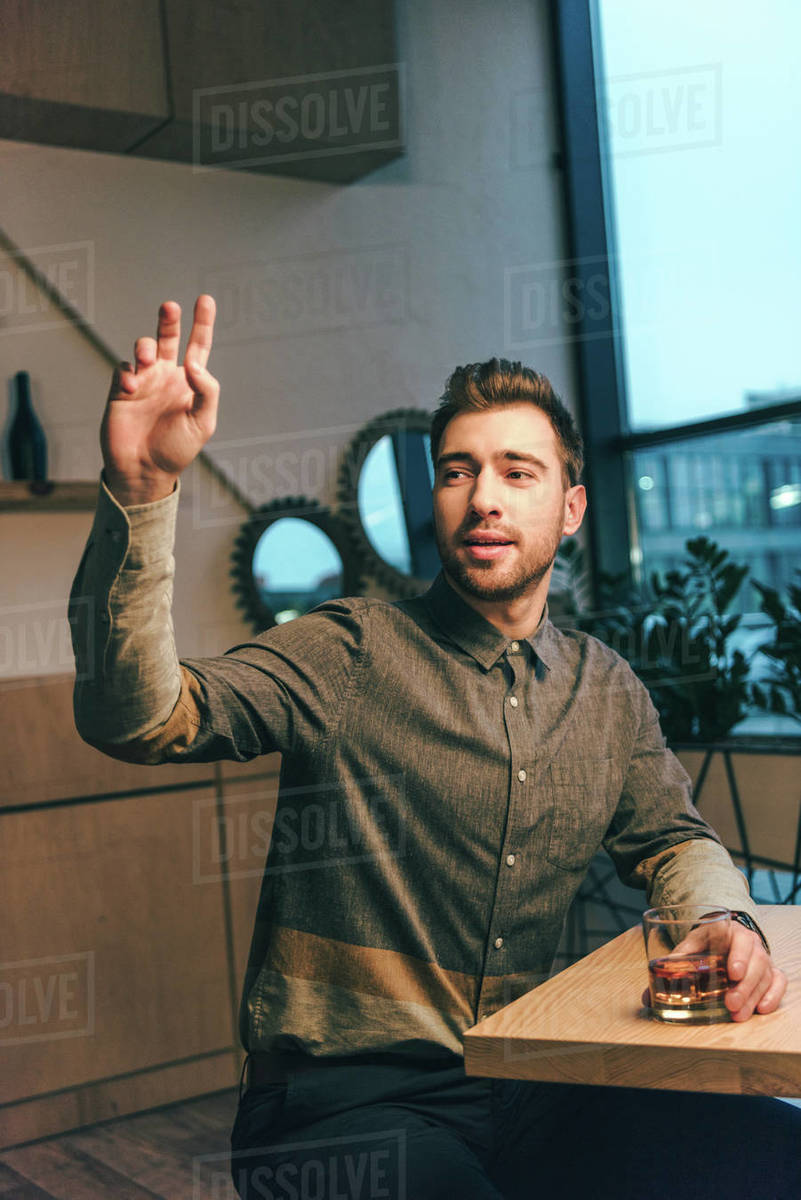 Portrait of man with glass of whiskey calling for waiter in cafe ...