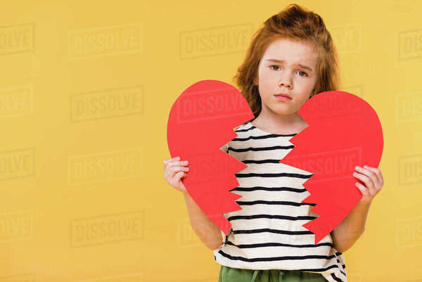 portrait of sad child with broken red paper heart isolated on yellow ...