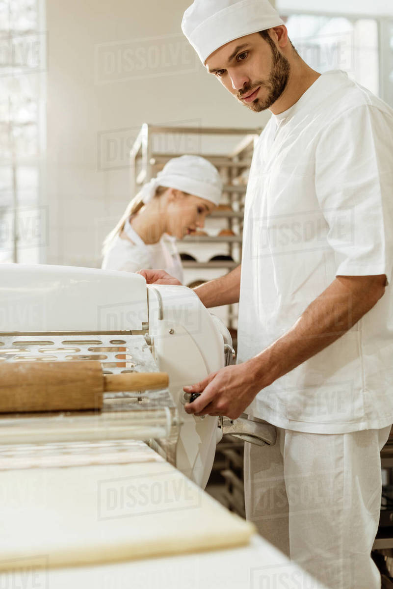 Handsome baker working with industrial dough roller at baking ...