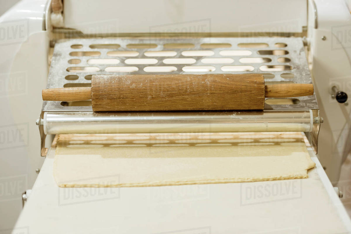 Close-up shot of industrial dough roller with traditional rolling pin ...