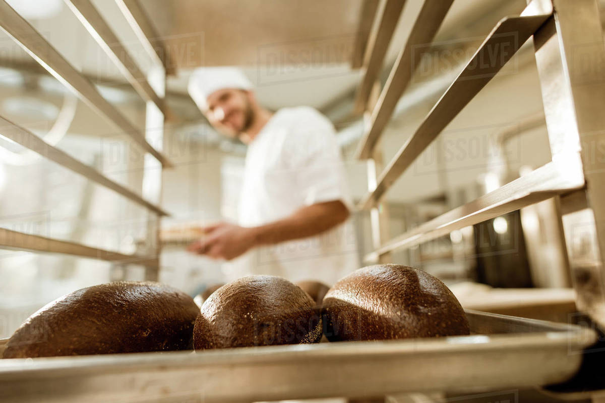 Happy baker looking at fresh loaves of bread on baking manufacture ...