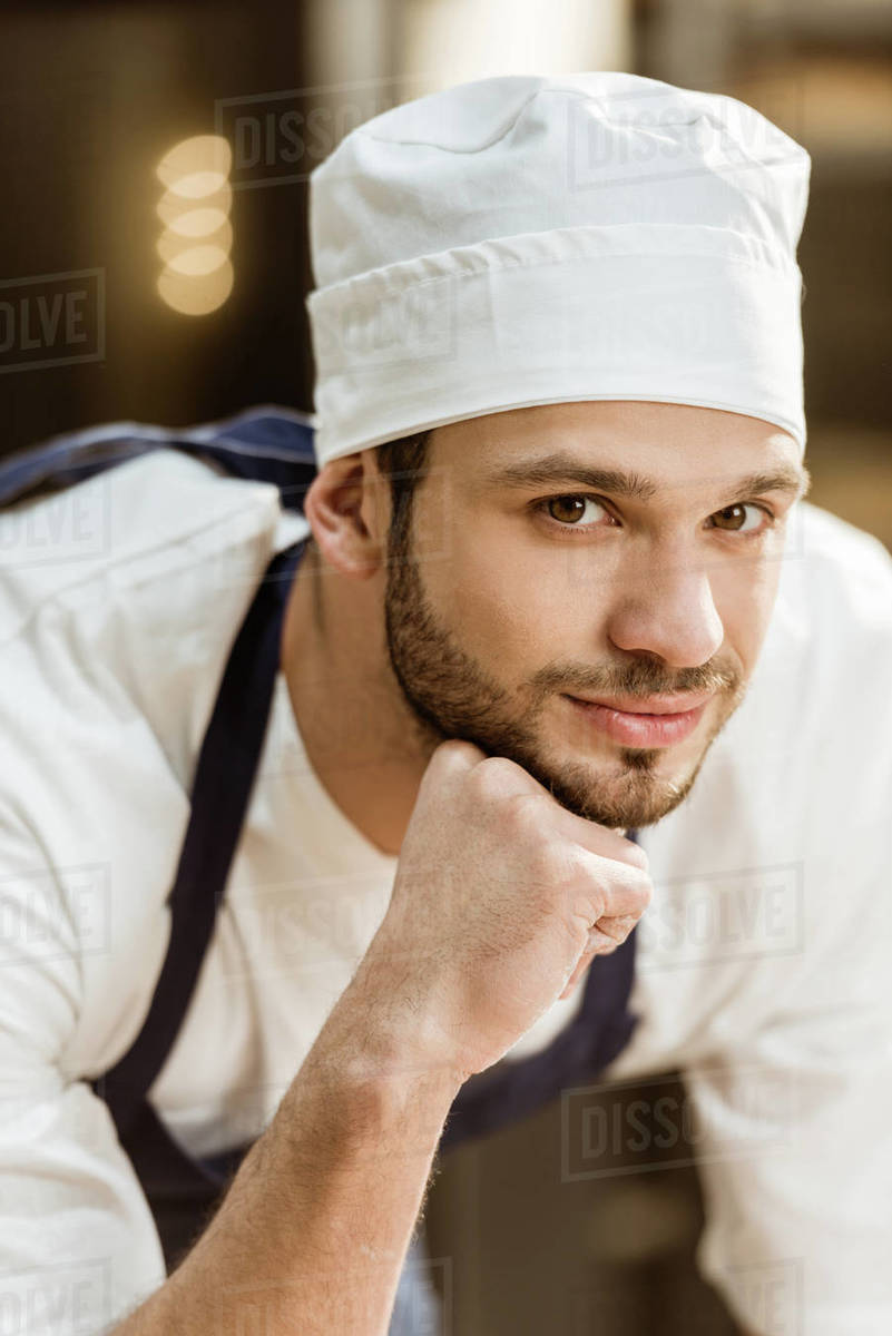 Close-up portrait of handsome young baker looking at camera on baking ...