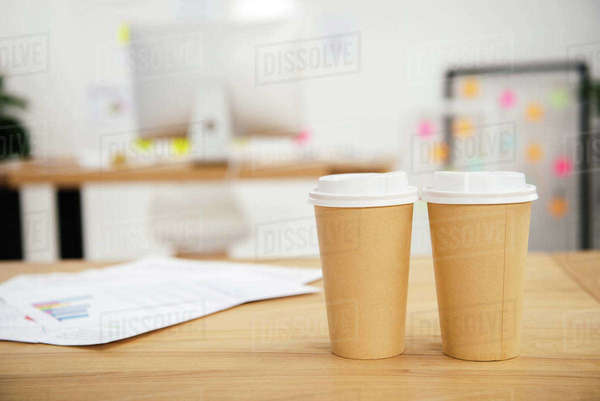 Close up view of disposable cups of coffee at workplace with papers in ...