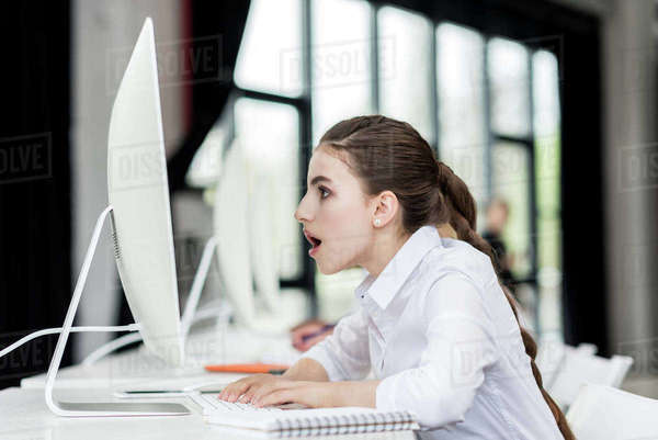 Side view of shocked teen girl looking at computer screen while ...