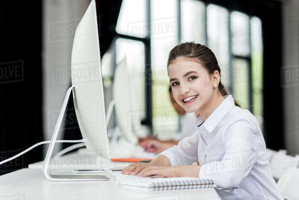 Side view of smiling teenage girl looking at camera while working on ...