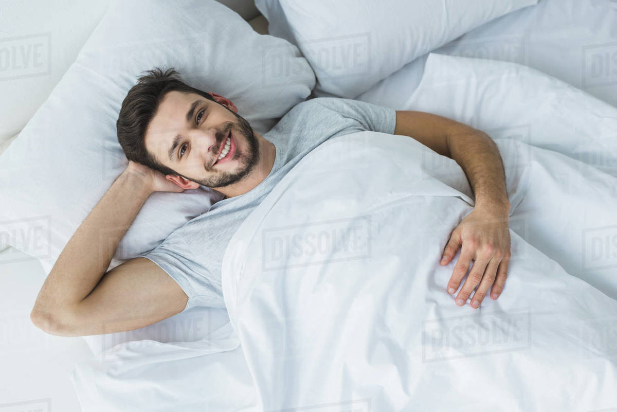 Top view of cheerful man lying on bed in the morning - Royalty-free ...