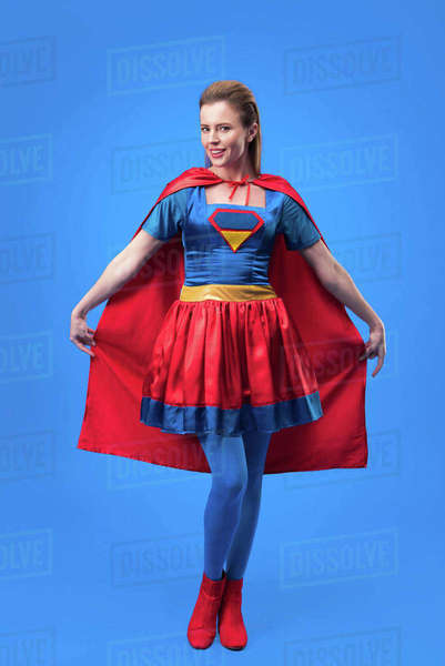 Attractive woman in superhero costume holding cape isolated on blue ...